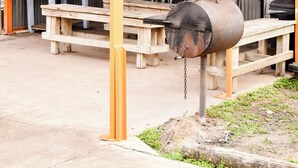 Uma área externa coberta com churrasqueira de metal, bancos de madeira e parede de metal corrugado.