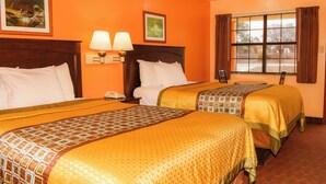 Quarto de hotel com duas camas, uma janela com cortinas, uma luminária e um quadro na parede.