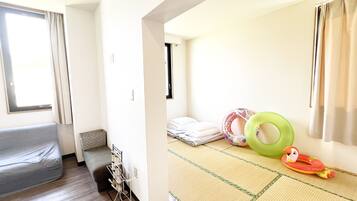Quarto com cama futon, sofá futon, uma pequena mesa e uma cadeira futon. Há duas camas futon visíveis.