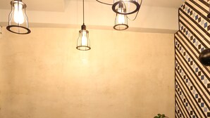 Quarto aconchegante com uma mesa de madeira, duas cadeiras, um pequeno alto-falante preto, uma revista, uma xícara de café e uma planta em uma mesinha lateral.