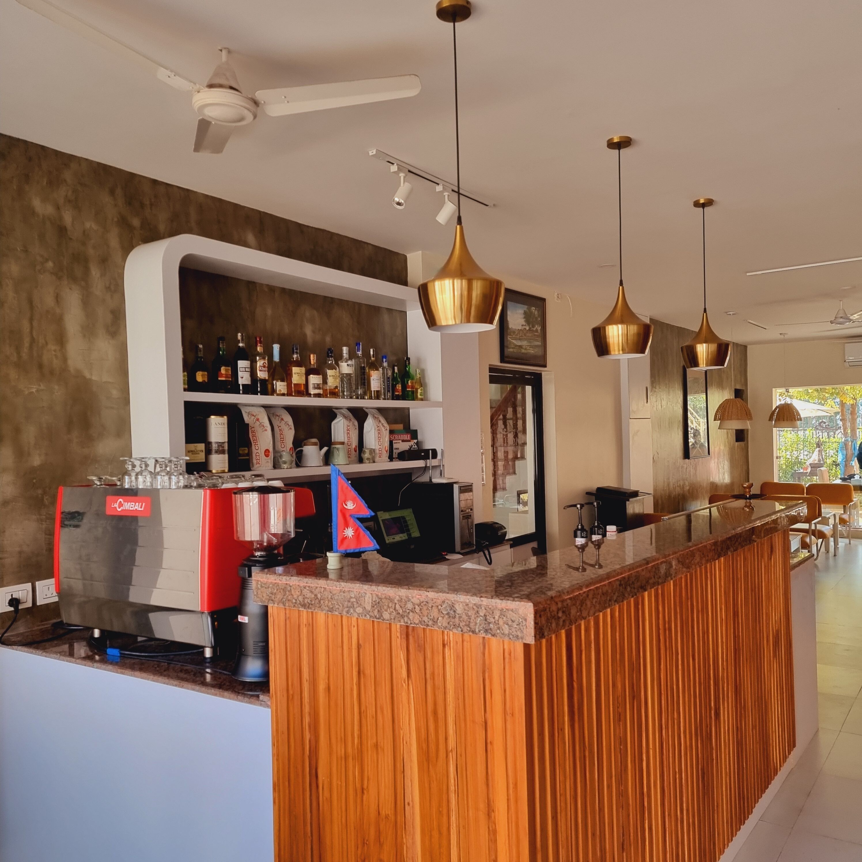 Uma área de bar com balcão de madeira, uma máquina de café e uma prateleira com diversos frascos.