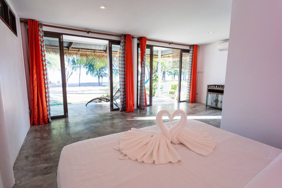 Quarto de hotel com uma cama, arranjo de toalha em formato de coração e vista para área externa por meio de grandes portas deslizantes.