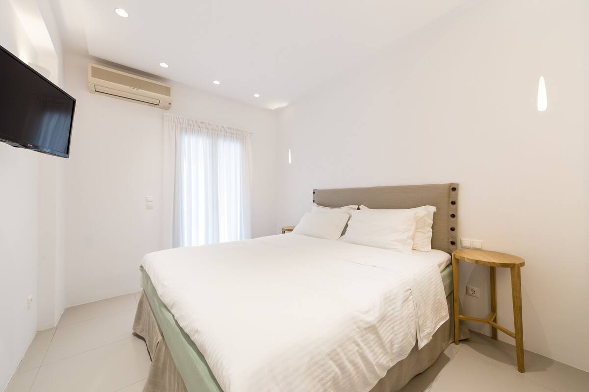 Quarto com cama, mesa de cabeceira, televisão fixada na parede e aparelho de ar condicionado.
