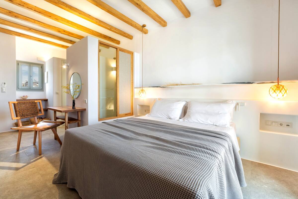 Quarto com cama, cadeira, mesa e espelho.