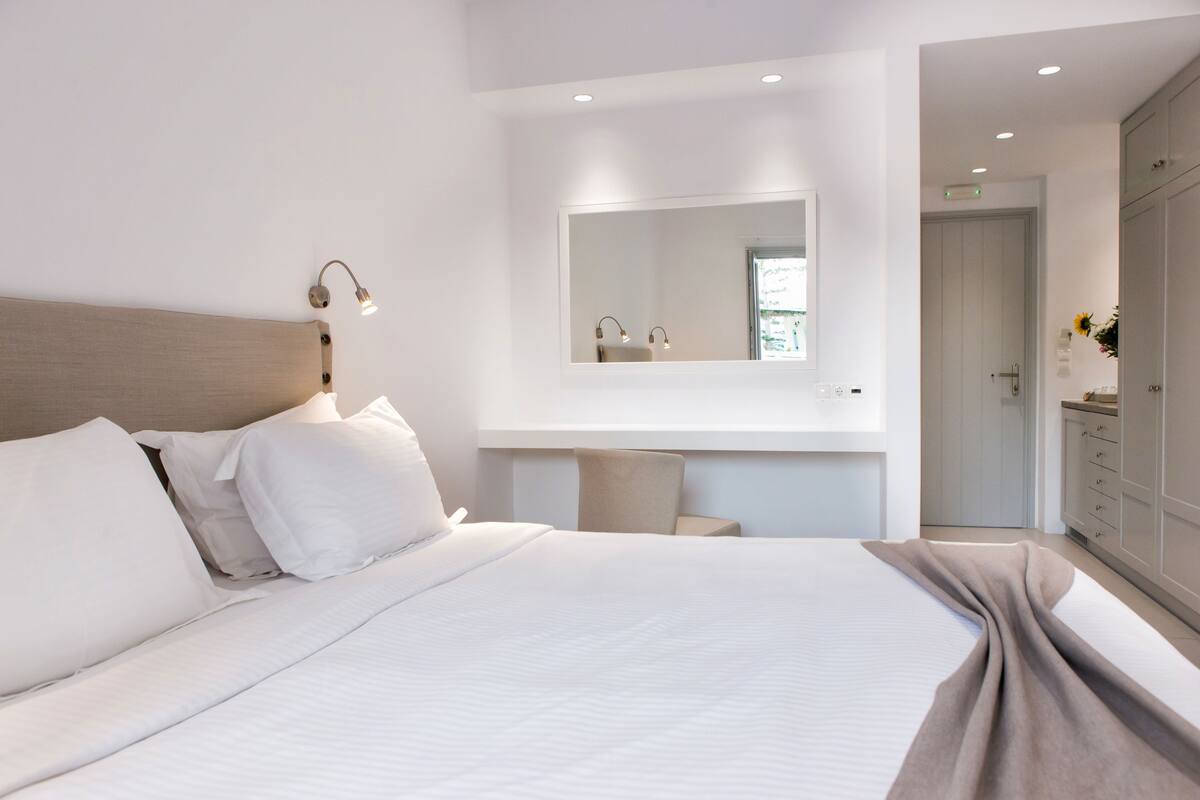 Quarto moderno com uma cama grande, mesa de cabeceira, espelho e guarda-roupa.