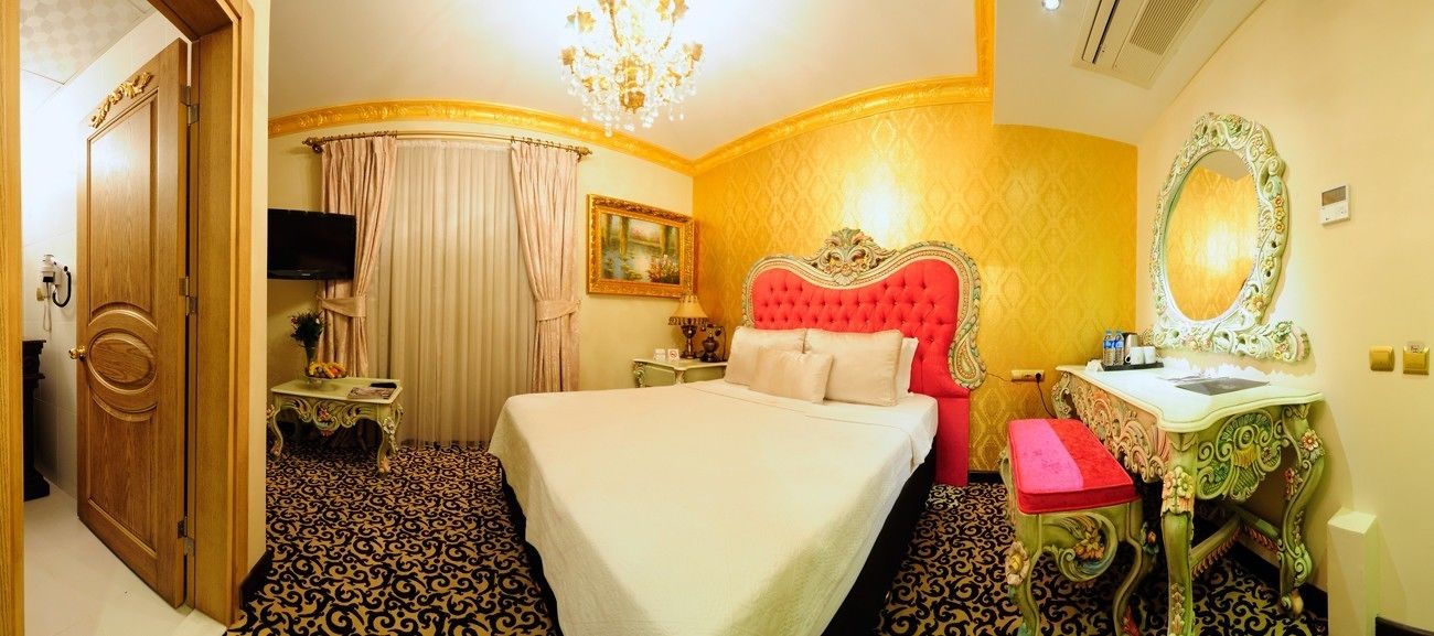 Quarto de hotel com uma cama grande, uma toucador com espelho, televisão e um candelabro.