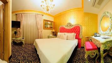 Quarto de hotel com uma cama grande, uma toucador com espelho, televisão e um candelabro.