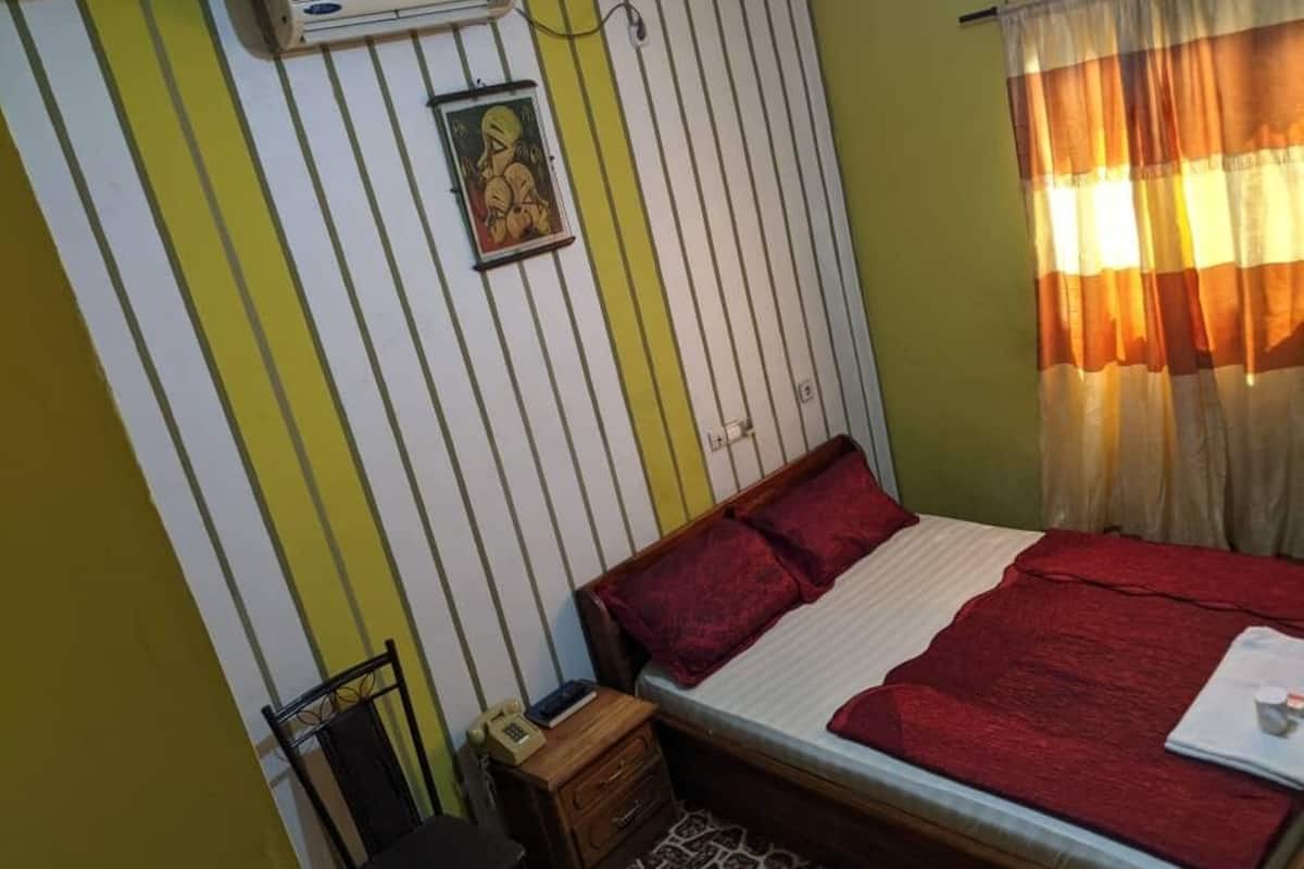 Quarto com cama, mesa de cabeceira, cadeira, ar-condicionado na parede e janela com cortinas.