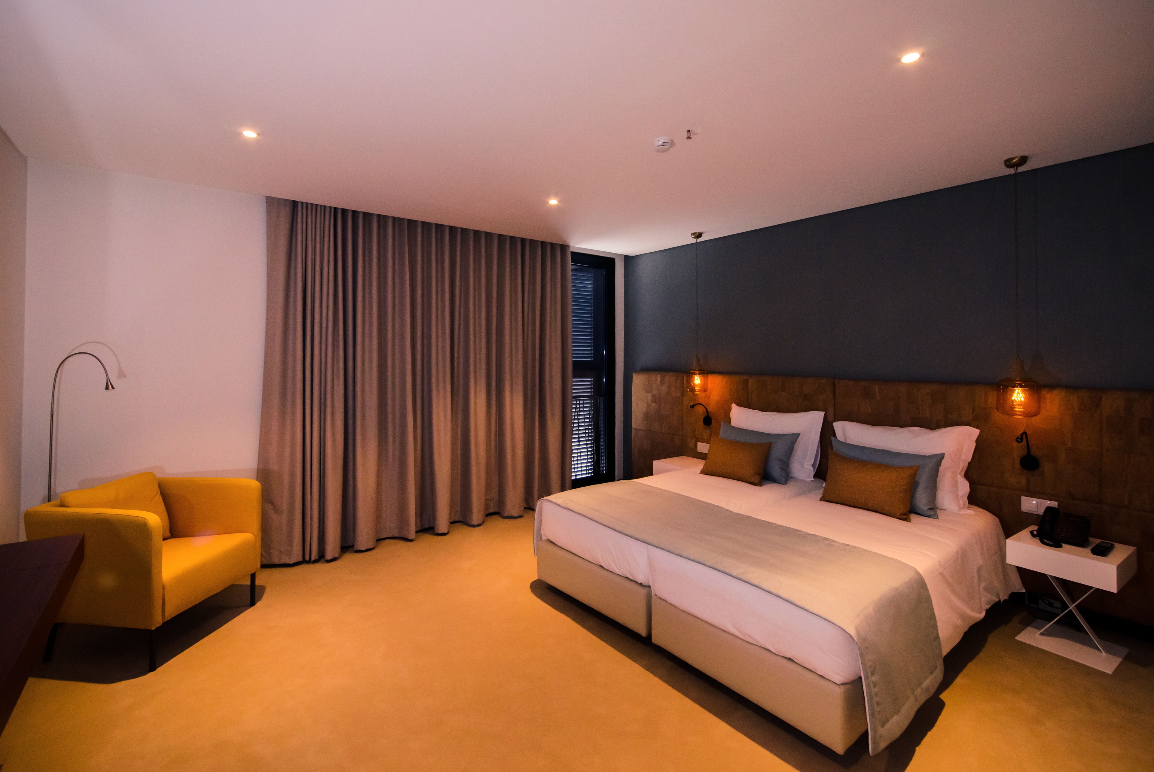 Quarto de hotel moderno com uma cama grande, um sofá, uma escrivaninha com telefone e uma janela com cortinas.