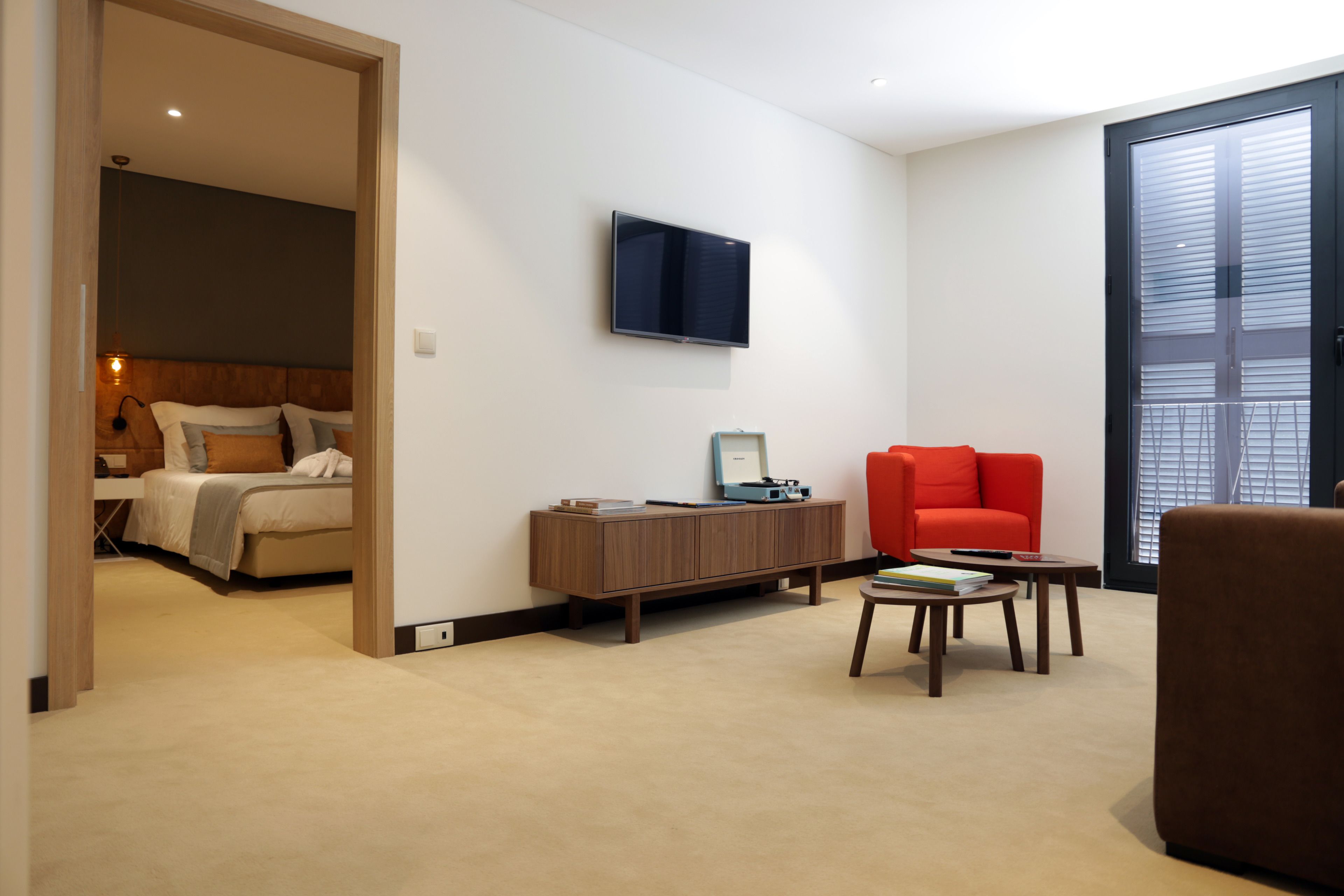 Uma sala de estar moderna com uma televisão de tela plana na parede, um sofá marrom, uma poltrona vermelha e uma pequena mesa de centro.