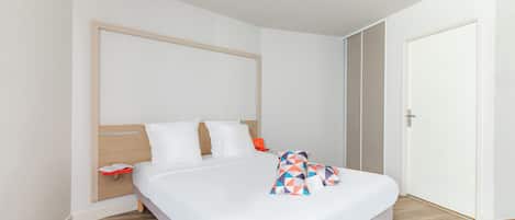 Quarto de hotel moderno com uma cama grande, cabeceira de madeira e mesa de cabeceira embutida.