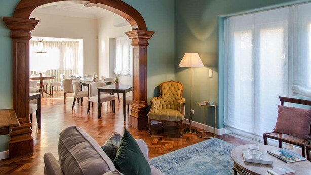 Uma sala de estar espaçosa com um arco de madeira, uma poltrona confortável, uma mesa de centro e uma área de jantar ao fundo.