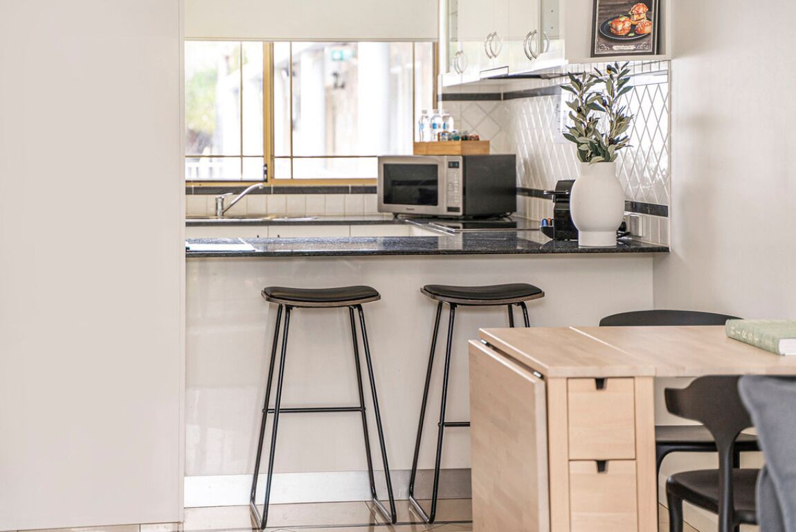 Uma cozinha moderna com micro-ondas, dois bancos altos, uma mesa de madeira e um vaso com planta.