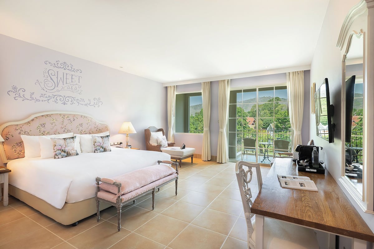 Quarto de hotel com uma cama grande, uma escrivaninha, uma cadeira, uma mesa de cabeceira e vista para o exterior.