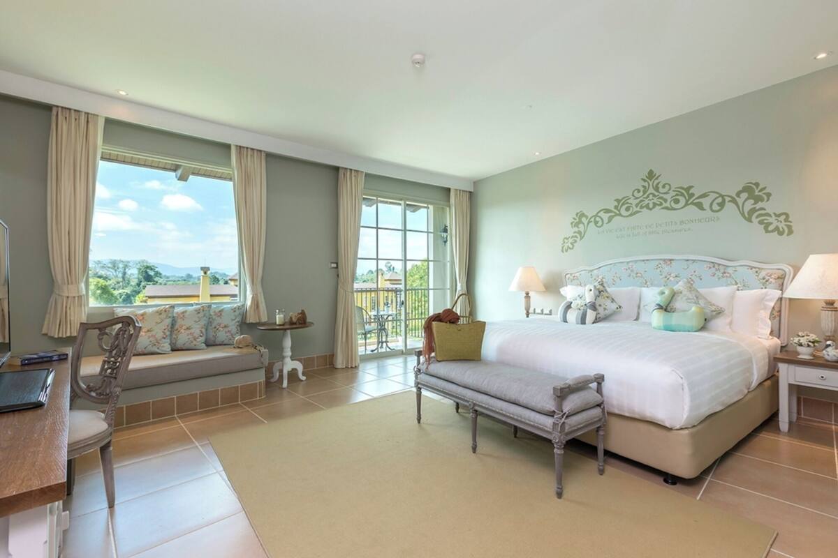 Um quarto espaçoso com uma cama grande, área de estar com mesa e varanda com vista.