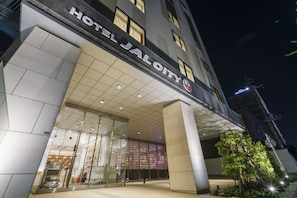 Entrada de hotel com design moderno, grandes portas de vidro e uma placa com a inscrição "HOTEL JALCITY".