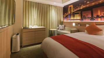 Quarto de hotel com cama, escrivaninha, cadeira, mesinha e televisão fixada na parede.