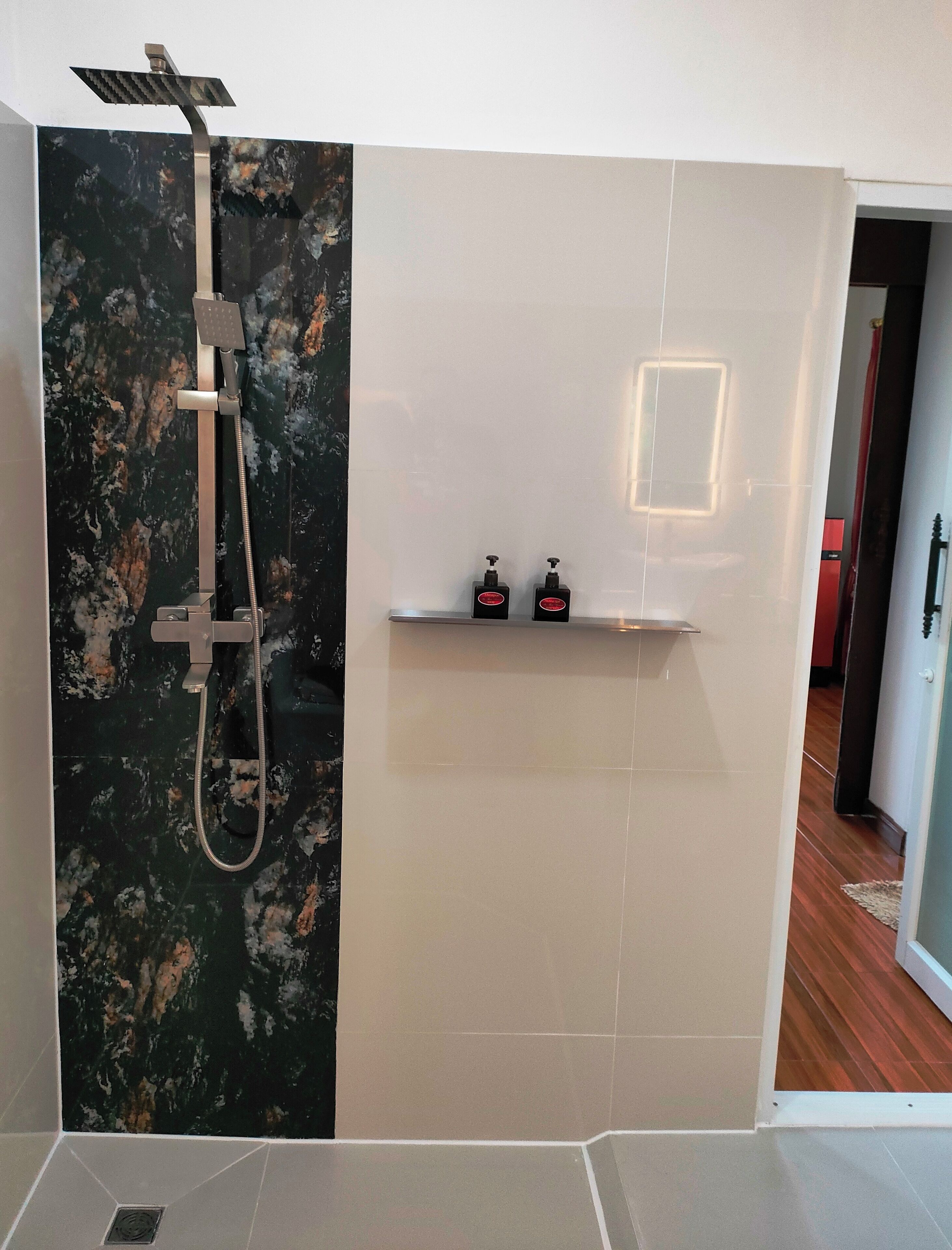 Uma casa de banho moderna com chuveiro, toucador com espelho e duas embalagens de sabonete.