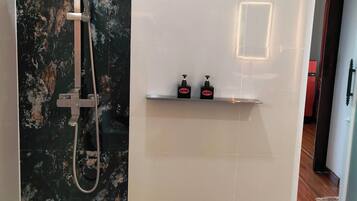 Uma casa de banho moderna com chuveiro, toucador com espelho e duas embalagens de sabonete.