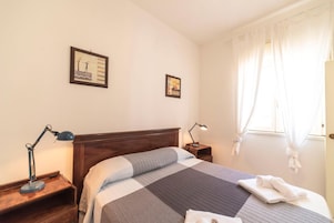 Quarto de hotel bem arrumado com uma cama, duas mesas de cabeceira, uma janela com cortinas e dois quadros na parede.