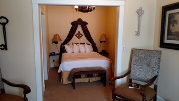 Quarto com uma cama de dossel, luminárias de cabeceira, um banco de madeira e uma cadeira com almofada estampada.