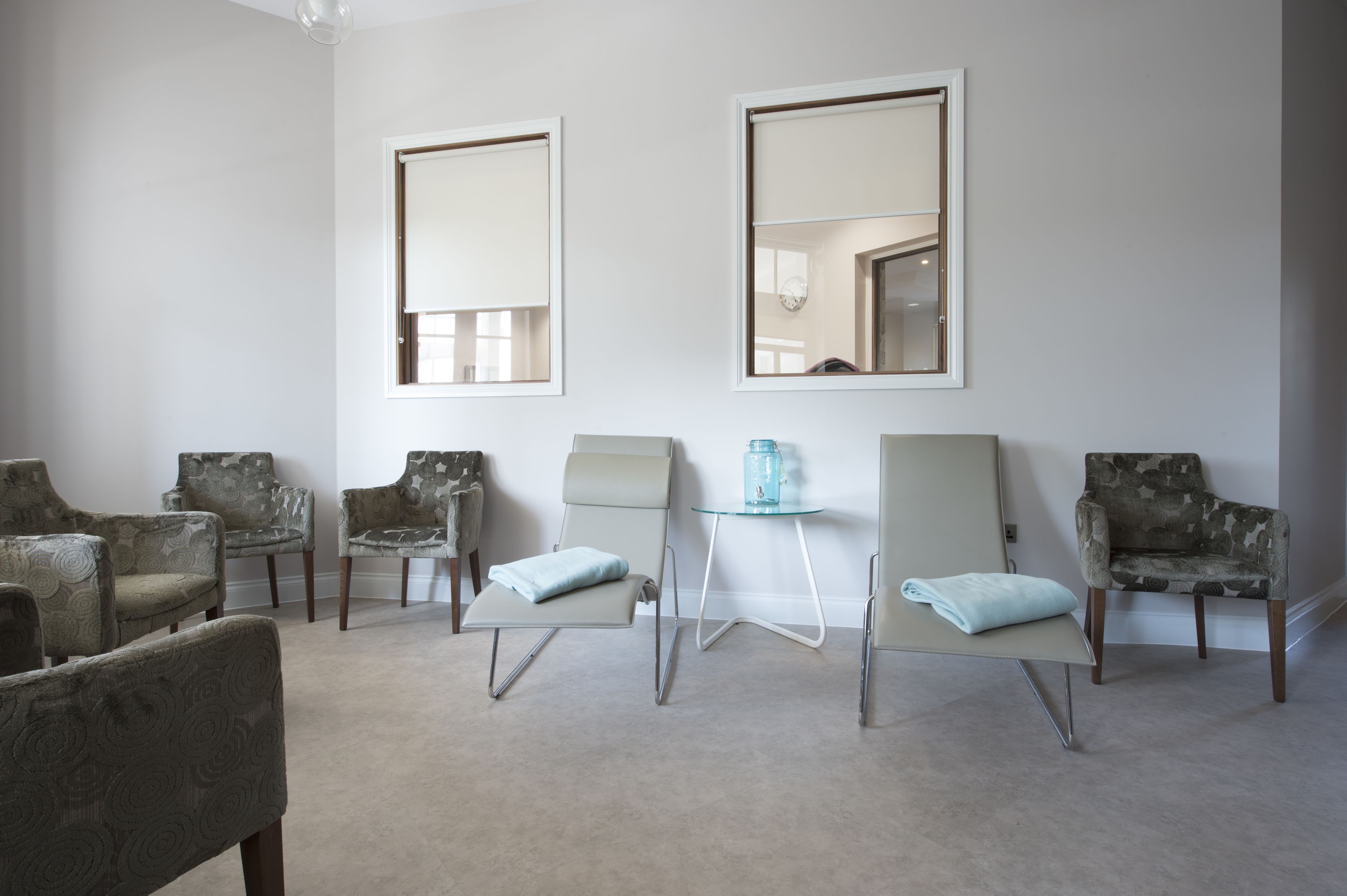 Um quarto com quatro poltronas, uma mesa de vidro e duas grandes espelhos nas paredes.
