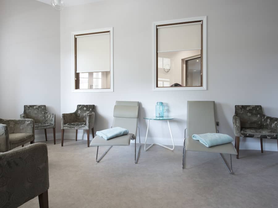 Um quarto com quatro poltronas, uma mesa de vidro e duas grandes espelhos nas paredes.