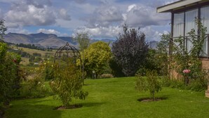 Um jardim com estufa, diversas plantas e vista para montanhas ao longe.