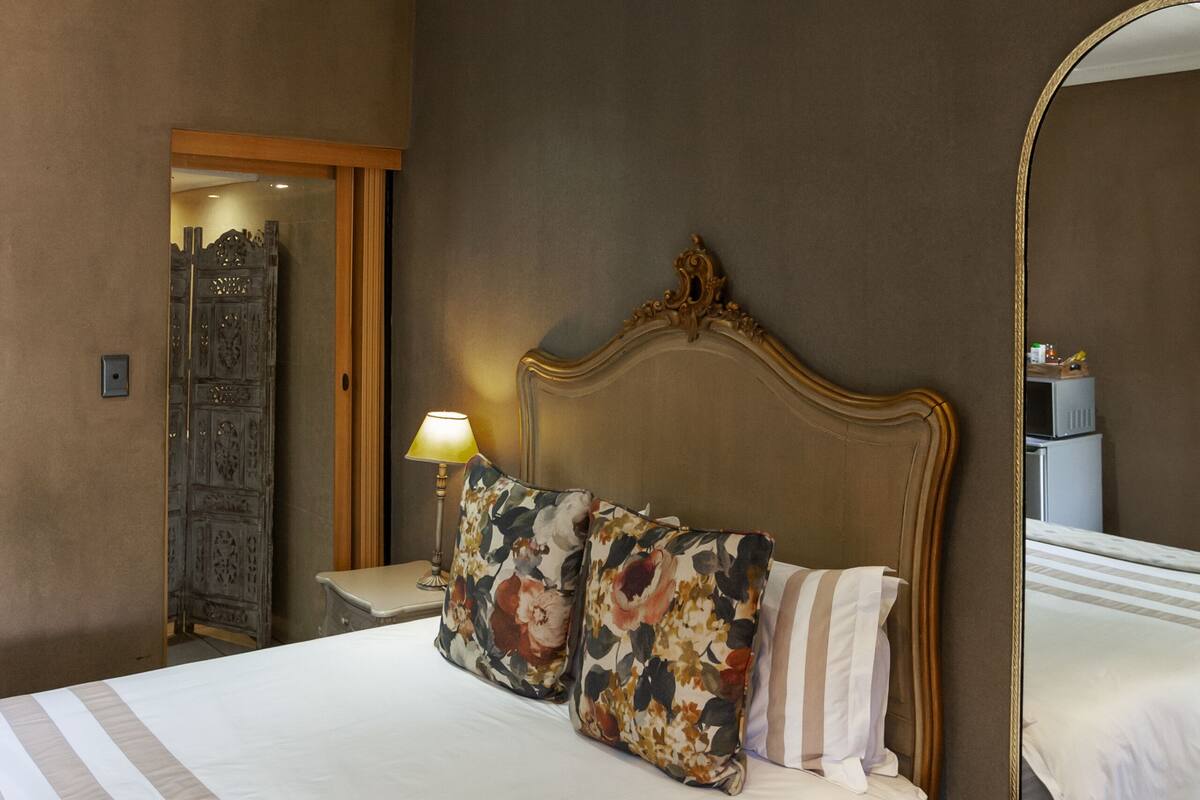 Quarto de hotel com uma cama grande, uma mesa de cabeceira de madeira, um espelho e um guarda-roupa.
