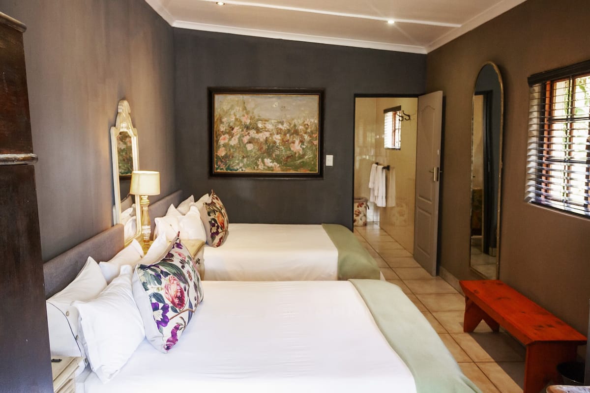 Quarto de hotel com duas camas, um banco, um quadro e um espelho.