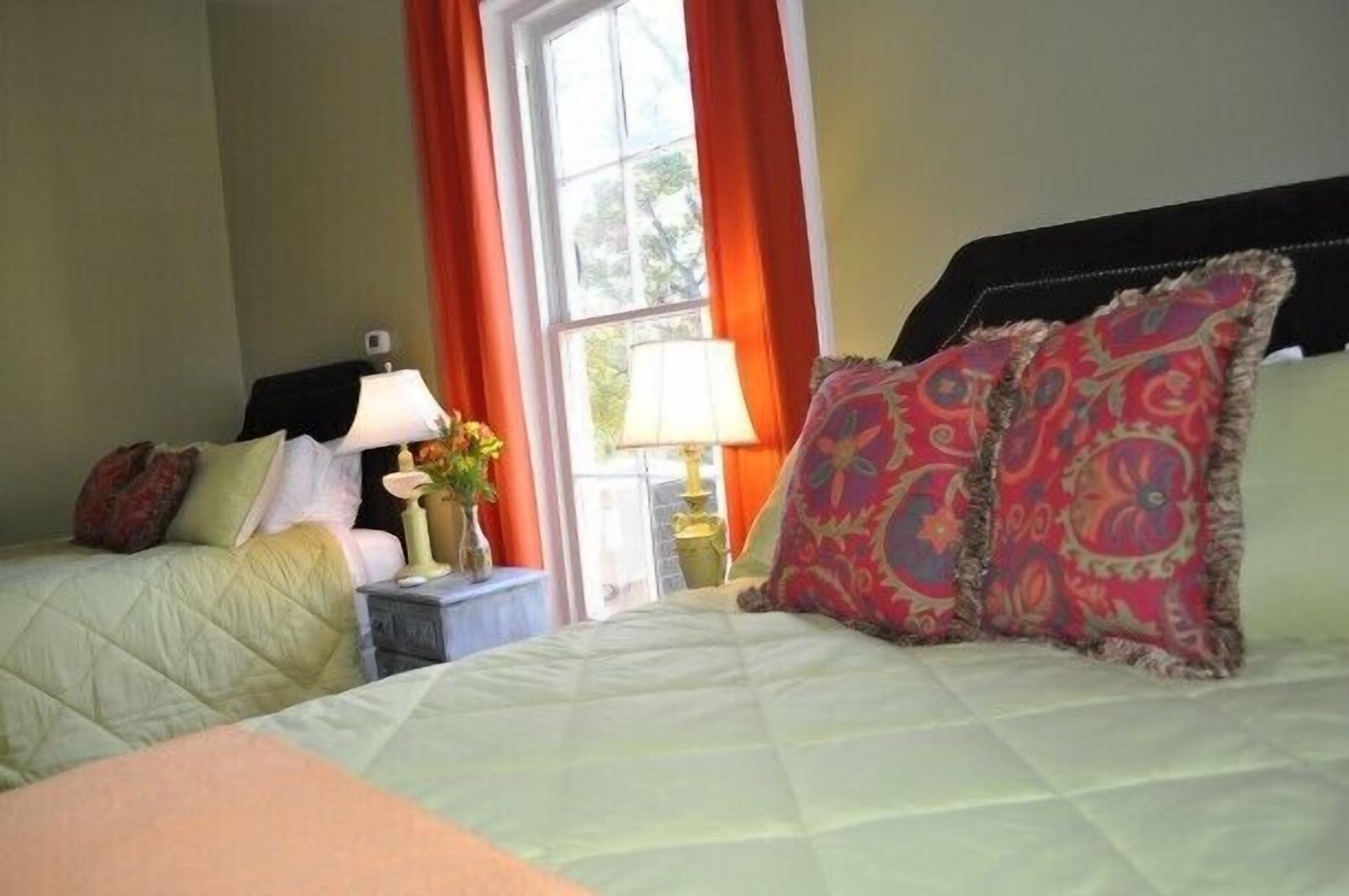 Quarto de hotel com cama, mesa de cabeceira, abajur e janela com cortinas.