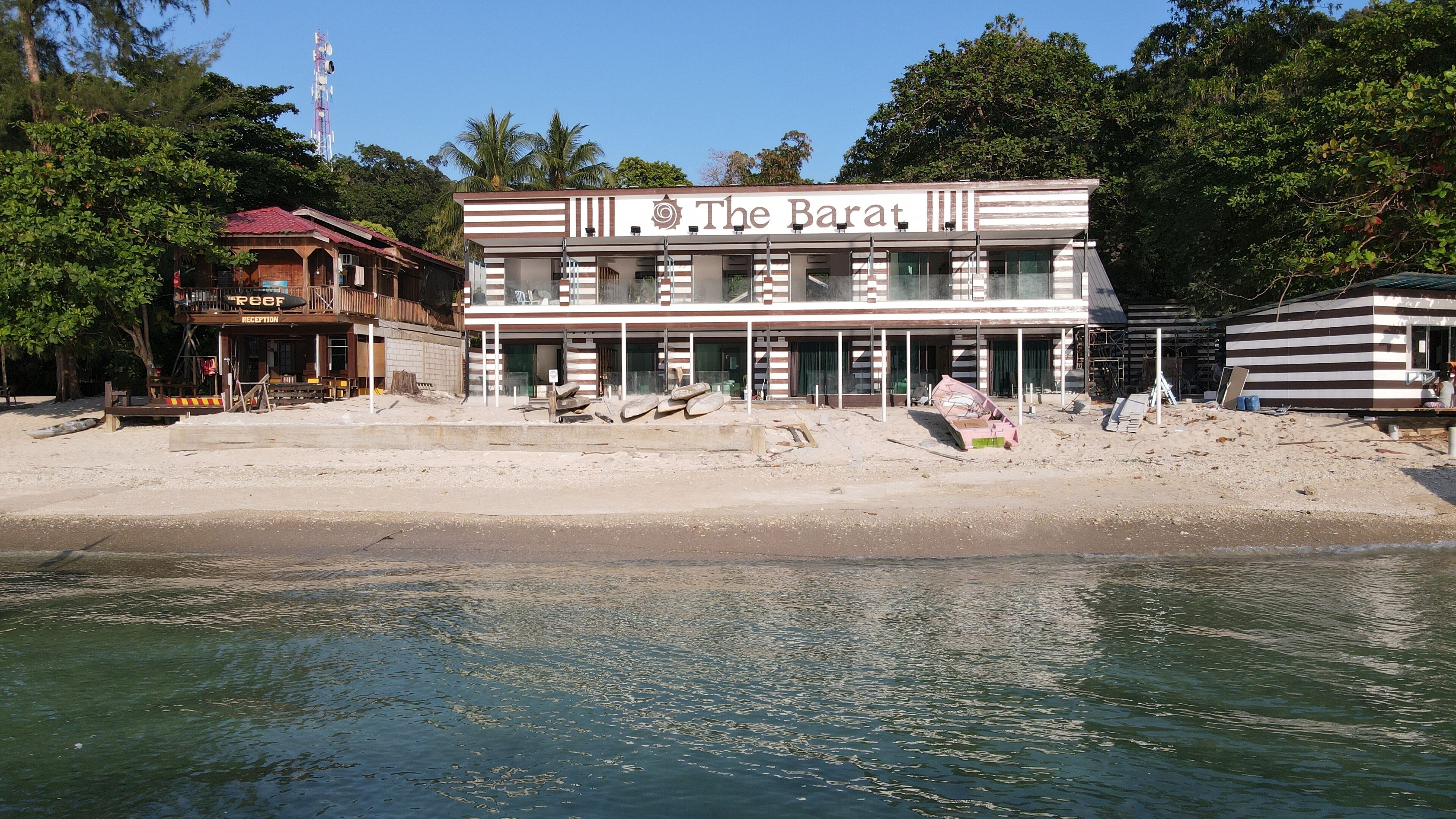 Um hotel na praia chamado 'The Barat', com área de recepção, vários quartos e vista para o mar.