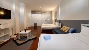 Quarto de hotel moderno com uma cama grande, um sofá, uma mesinha, uma televisão e um guarda-roupa.