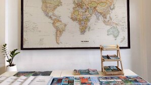 Um mapa-múndi na parede, uma planta pequena e um suporte de madeira com revistas.