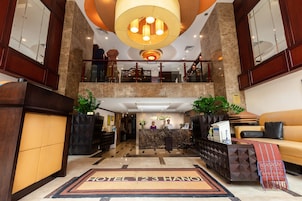 Um saguão de hotel com balcão de recepção, um sofá e uma escadaria para o andar superior.