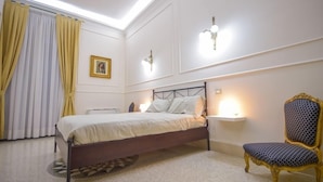 Quarto com cama, uma cadeira, mesa de cabeceira e um quadro na parede.