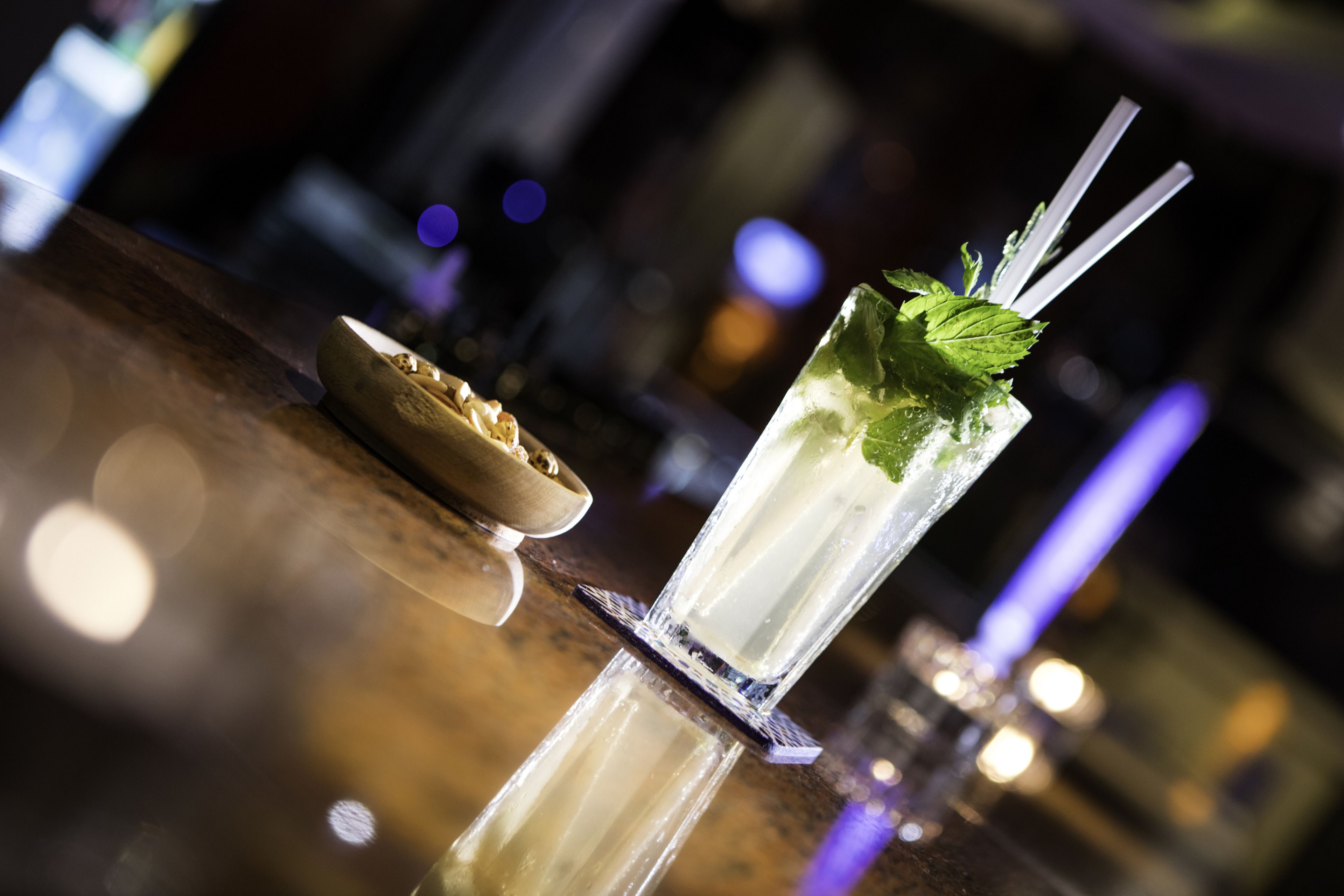 Um copo de cocktail com folha de hortelã e canudos sobre uma superfície refletora, provavelmente um balcão de bar.