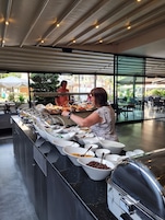 Buffet externo com diversos alimentos e uma churrasqueira.