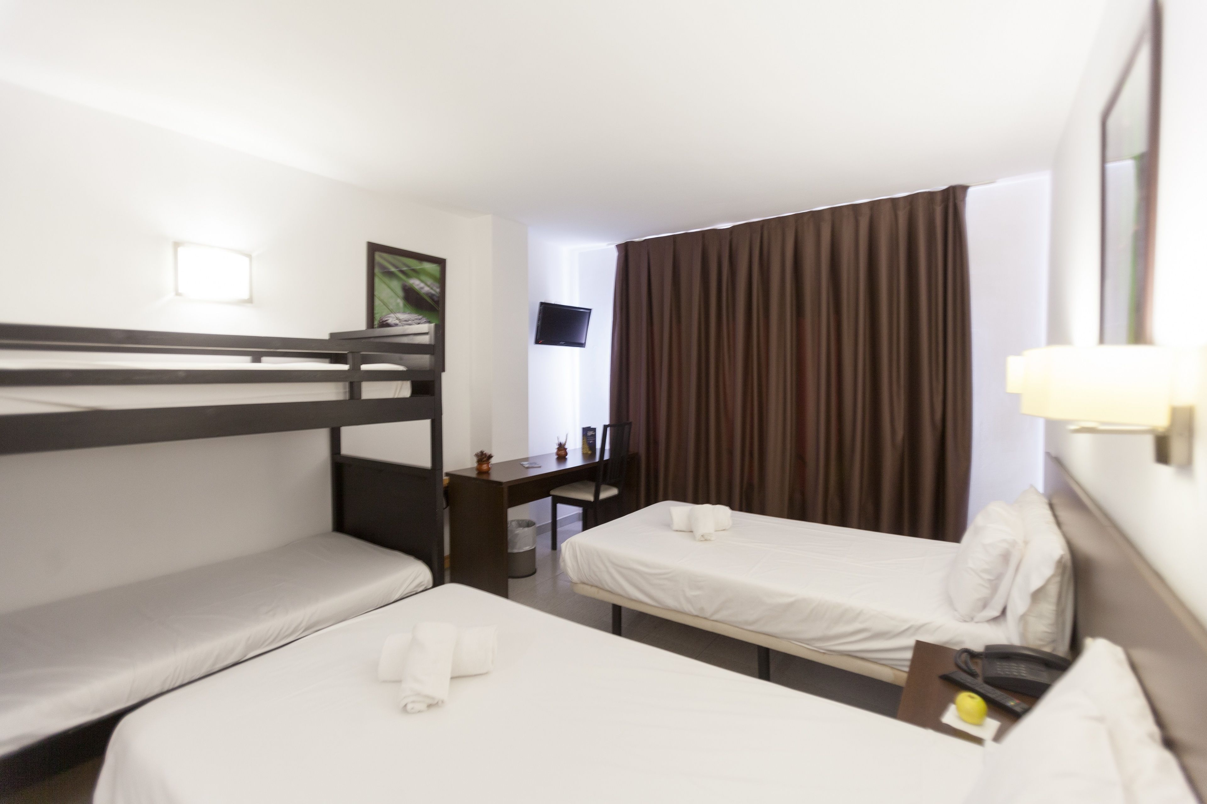 Quarto de hotel com duas camas de solteiro, uma escrivaninha com cadeira, televisão e janela com cortinas.
