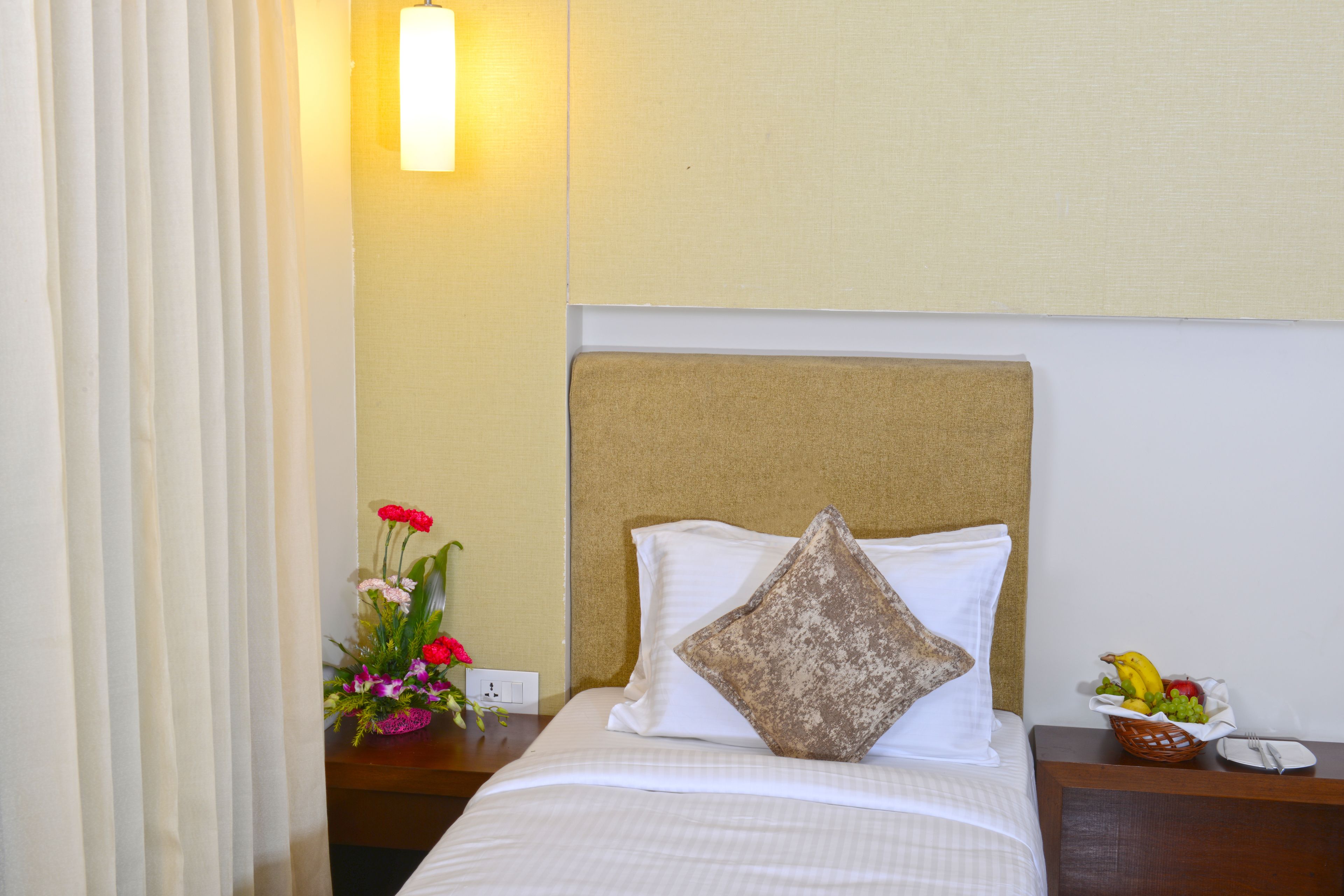 Cama bem arrumada com travesseiro, mesa de cabeceira com cesta de frutas e um vaso de flores.