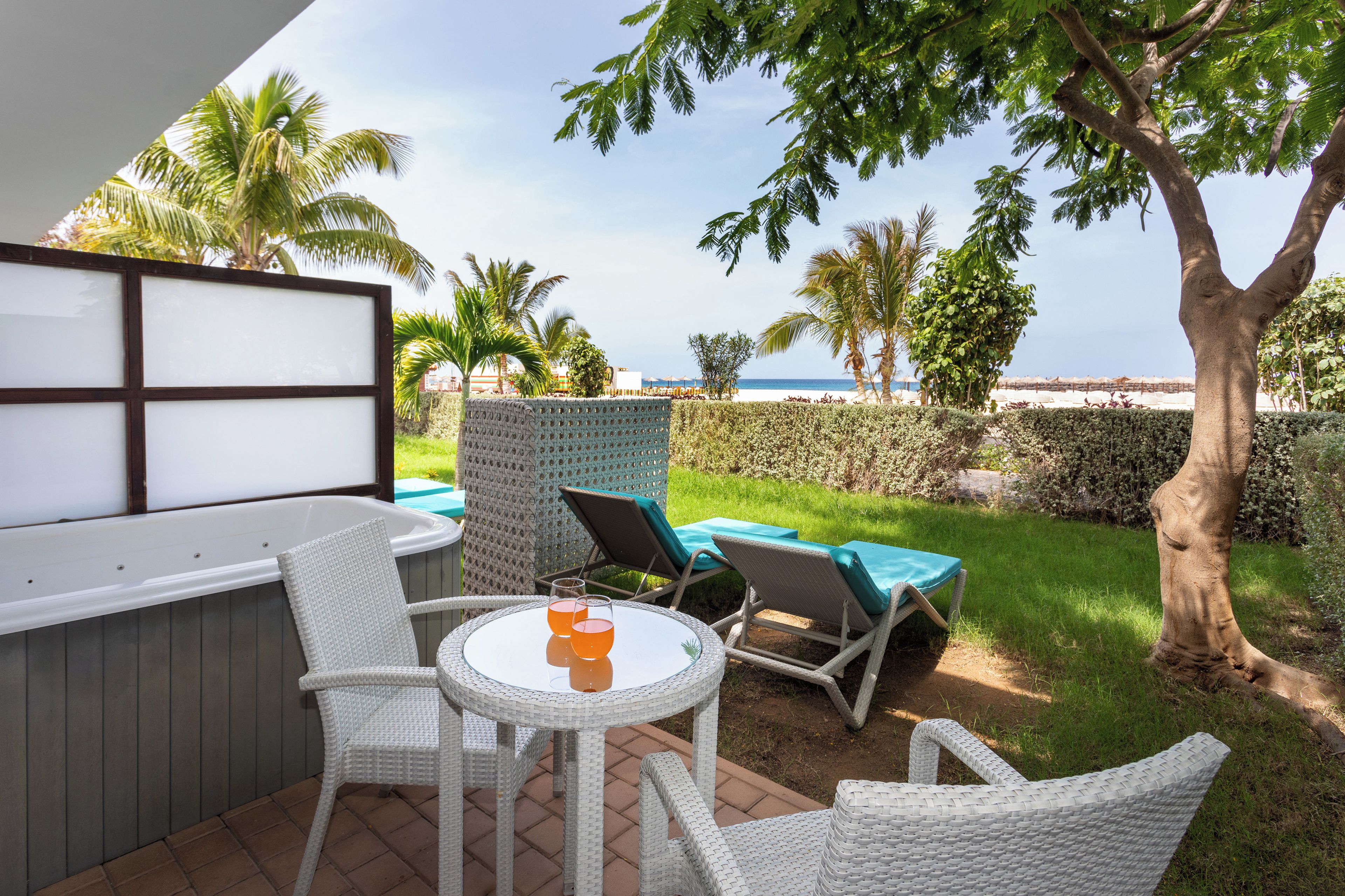 Uma área externa com assentos de vime, uma mesa de vidro e vista para o mar.