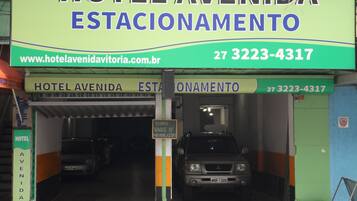 Entrada de hotel com uma placa indicando 'HOTEL AVENIDA ESTACIONAMENTO' e o endereço do site 'www.hotelavenidavistaoria.com.br'.