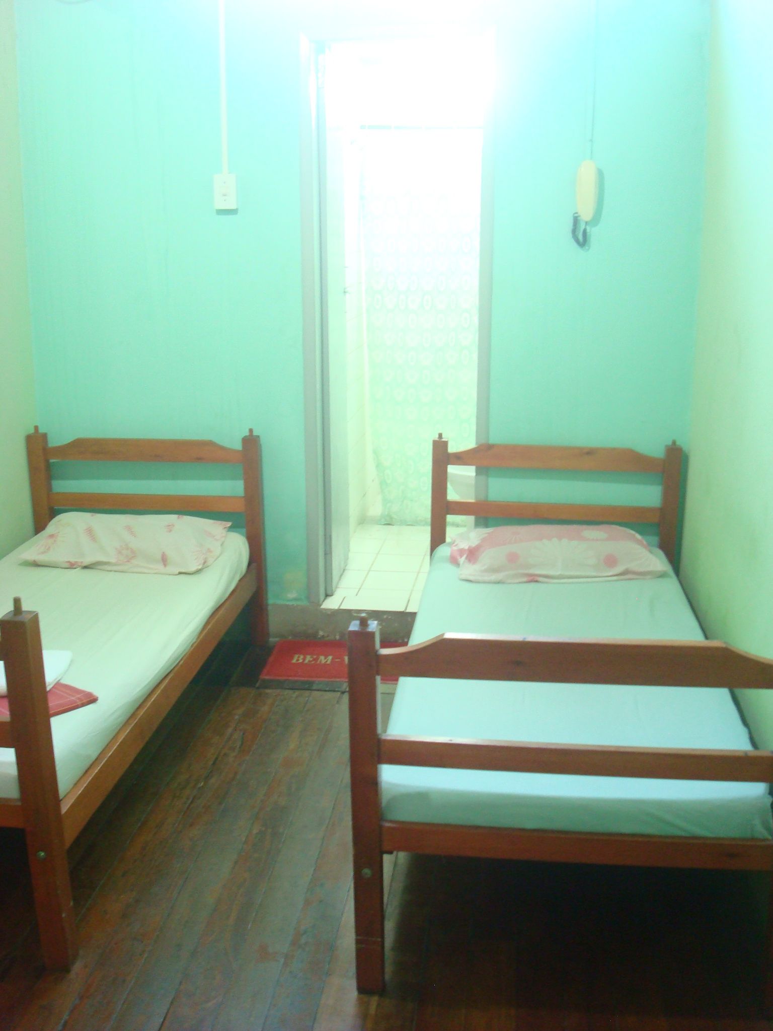 Um quarto com duas beliches de madeira, uma pequena janela com cortina e um tapete vermelho no chão.