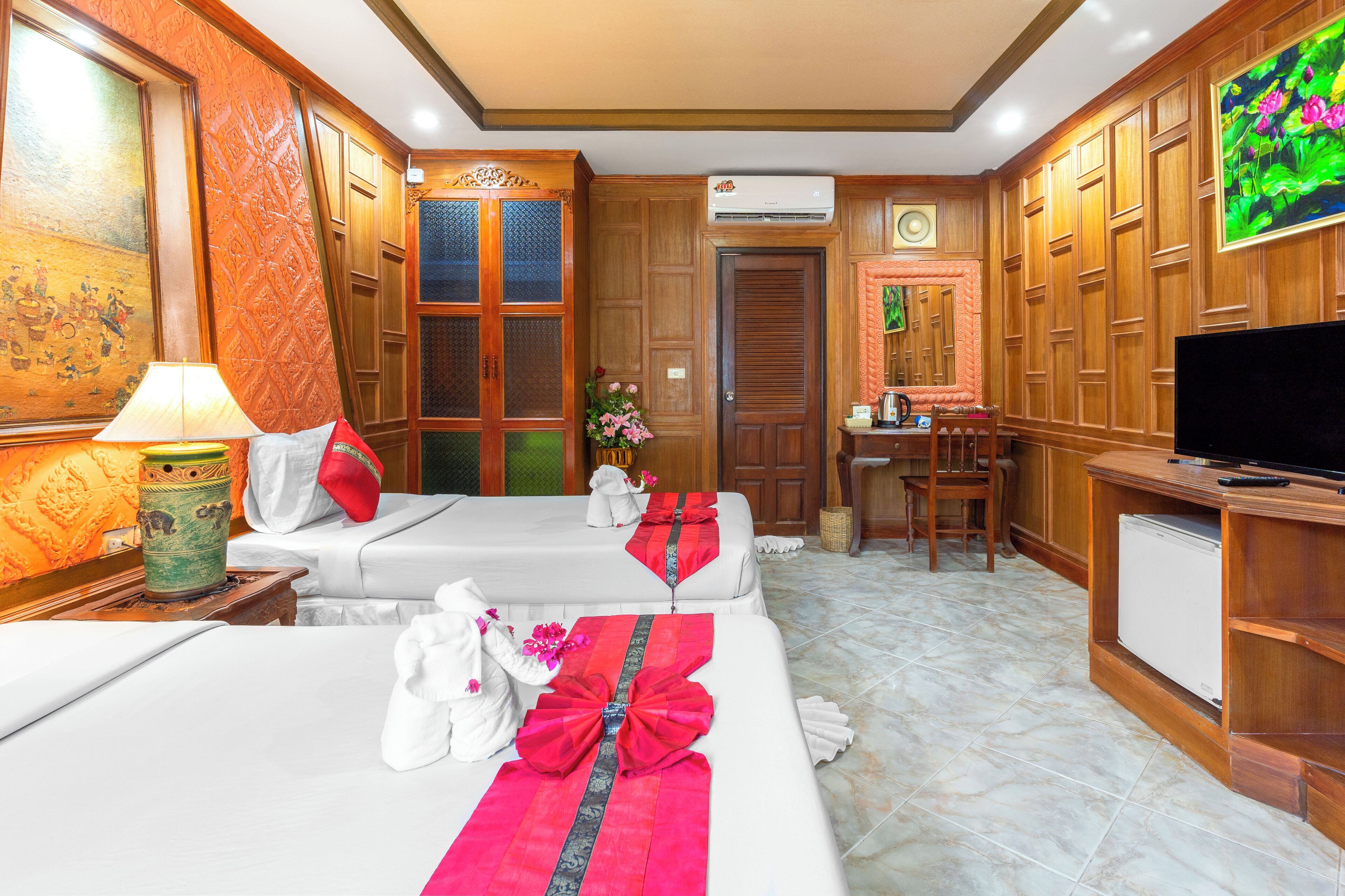 Quarto de hotel com duas camas, televisão, escrivaninha e um pequeno frigorífico.
