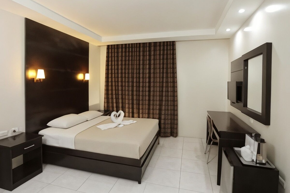 Quarto de hotel moderno com cama, mesas de cabeceira, escrivaninha e espelho.