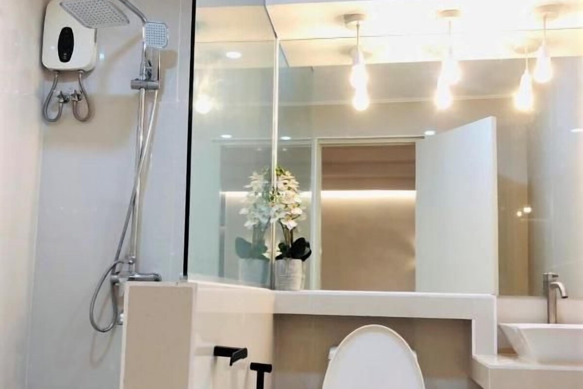 Uma casa de banho moderna com sanita, lavatório, chuveiro e um espelho grande.