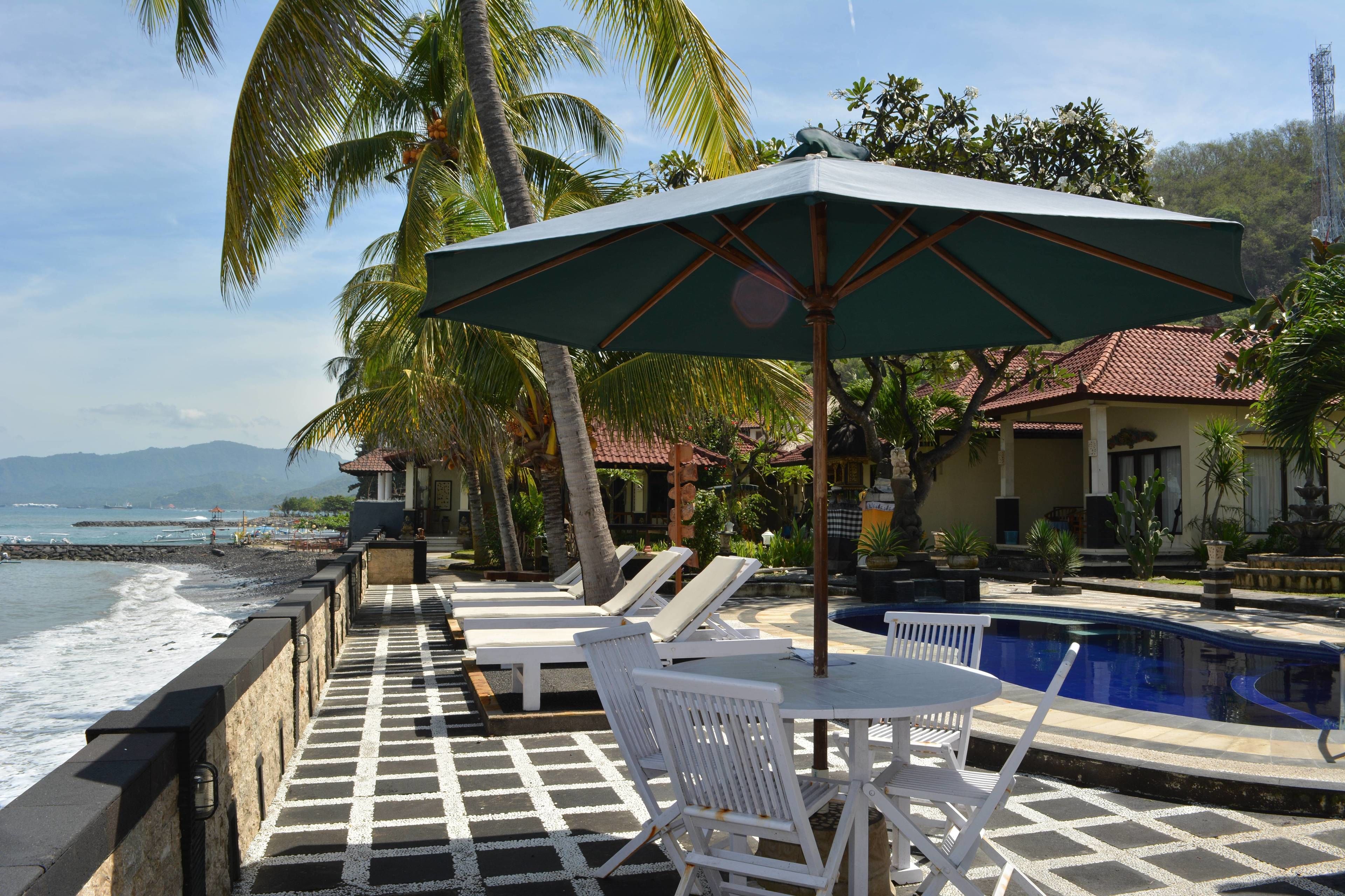 Área da piscina com espreguiçadeiras e um guarda-sol, com vista para o oceano.
