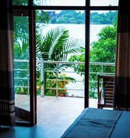 Quarto com uma grande porta de correr de vidro que dá para uma varanda com vista para a água e vegetação.