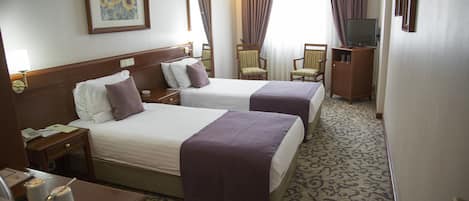 Quarto de hotel com duas camas, uma escrivaninha, uma cadeira, uma televisão e um quadro na parede.