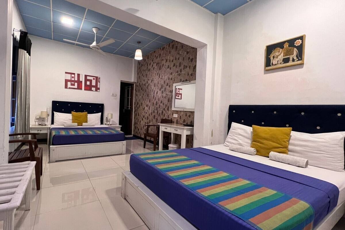 Quarto de hotel com duas camas, uma escrivaninha, uma cadeira e uma mesinha.